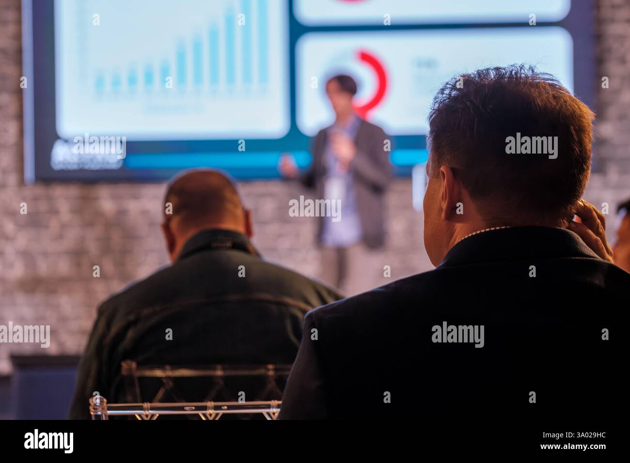 Attendees focus on a business presentation, analyzing projected charts ...
