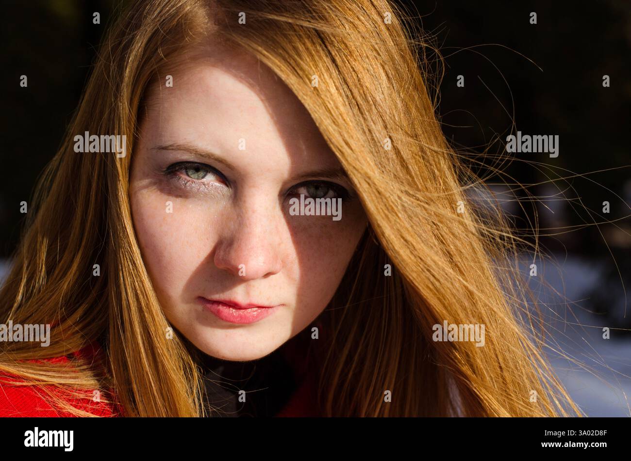 Young woman with red hair stares intensely, half in shadow, bright ...