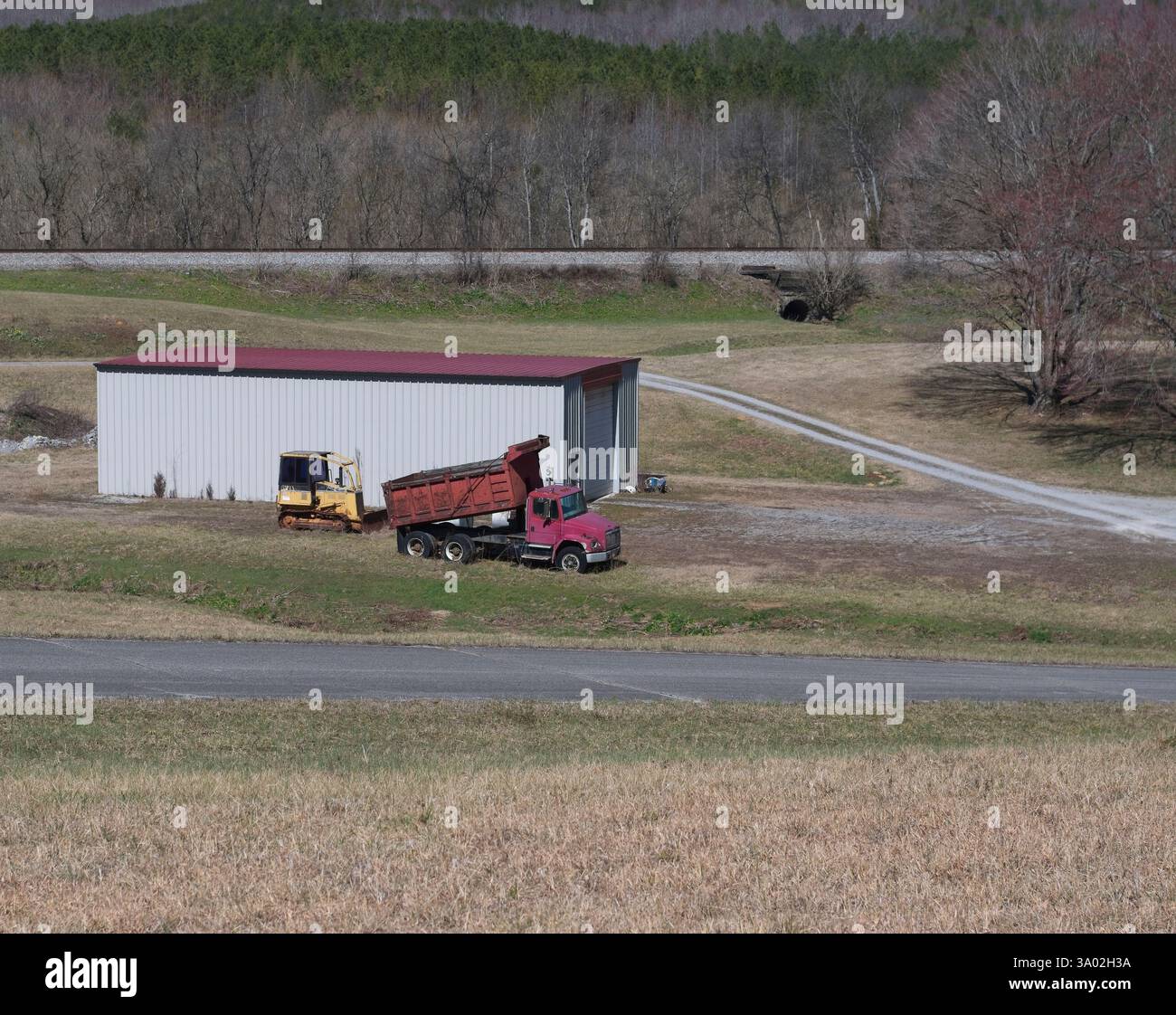 Country scene with dump truck and bulldozer against a metal building ...