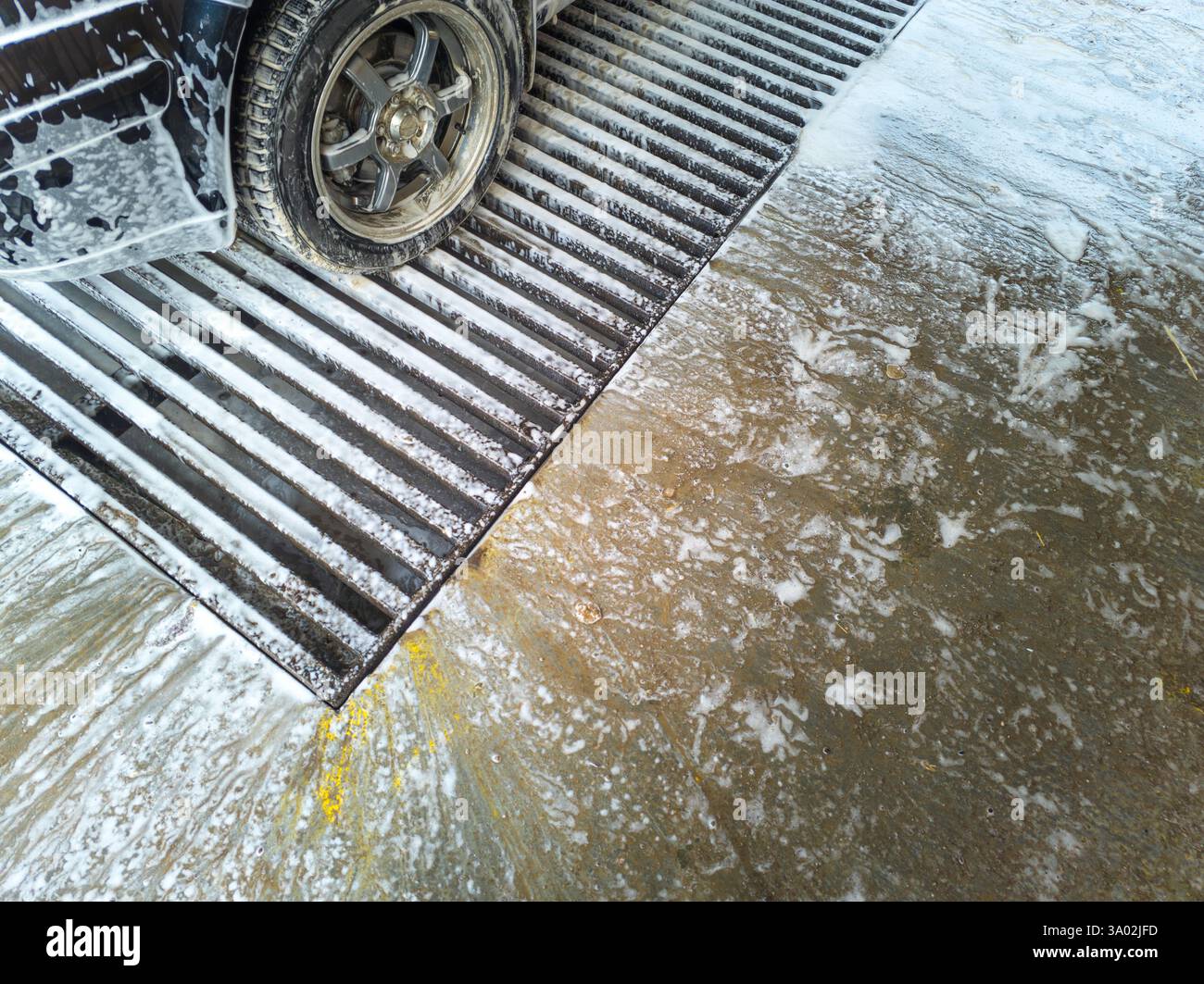 Soap sud waste flows to floor drain grid in car washing garage, close ...