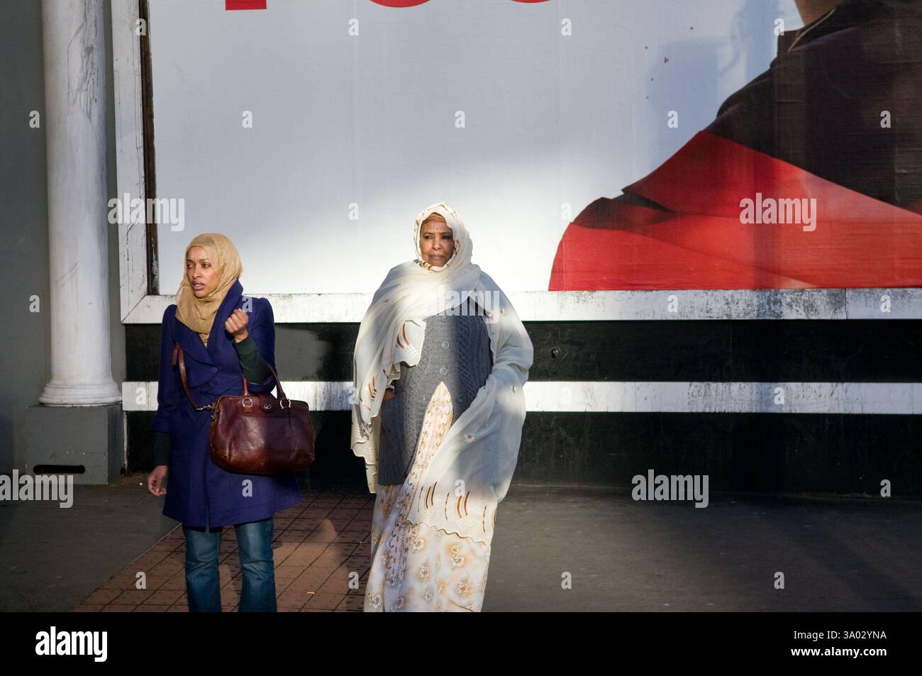 Two women, veiled, walk near a large billboard in a city street Stock ...
