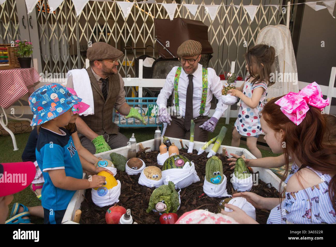 Children interact with decorated vegetables in a garden play area. A ...