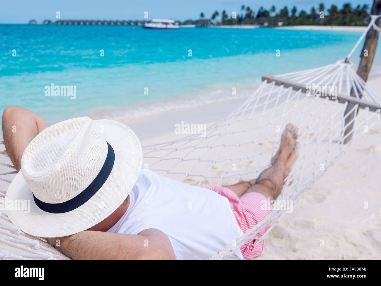 A young man in shorts and a T-shirt is lying in a hammock on the beach ...