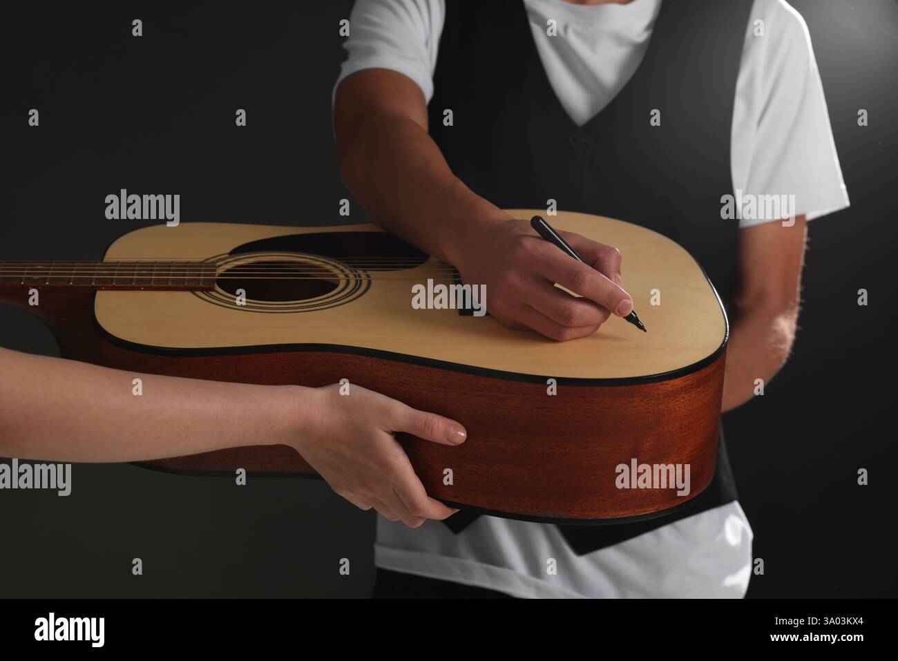 Musician signing autograph on guitar against dark background, closeup ...