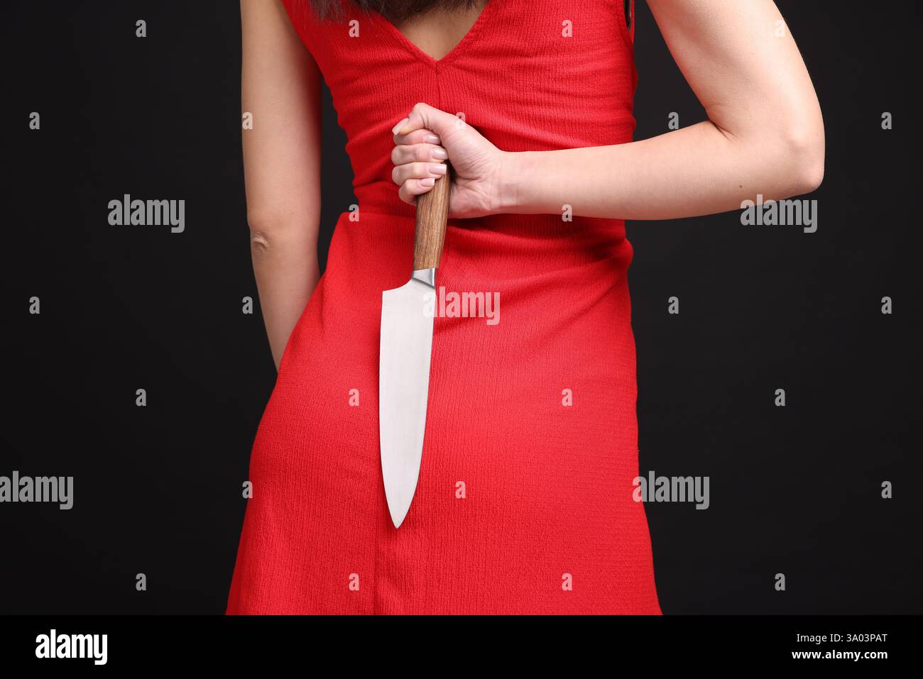 Businesswoman with knife behind her back on black background, closeup ...