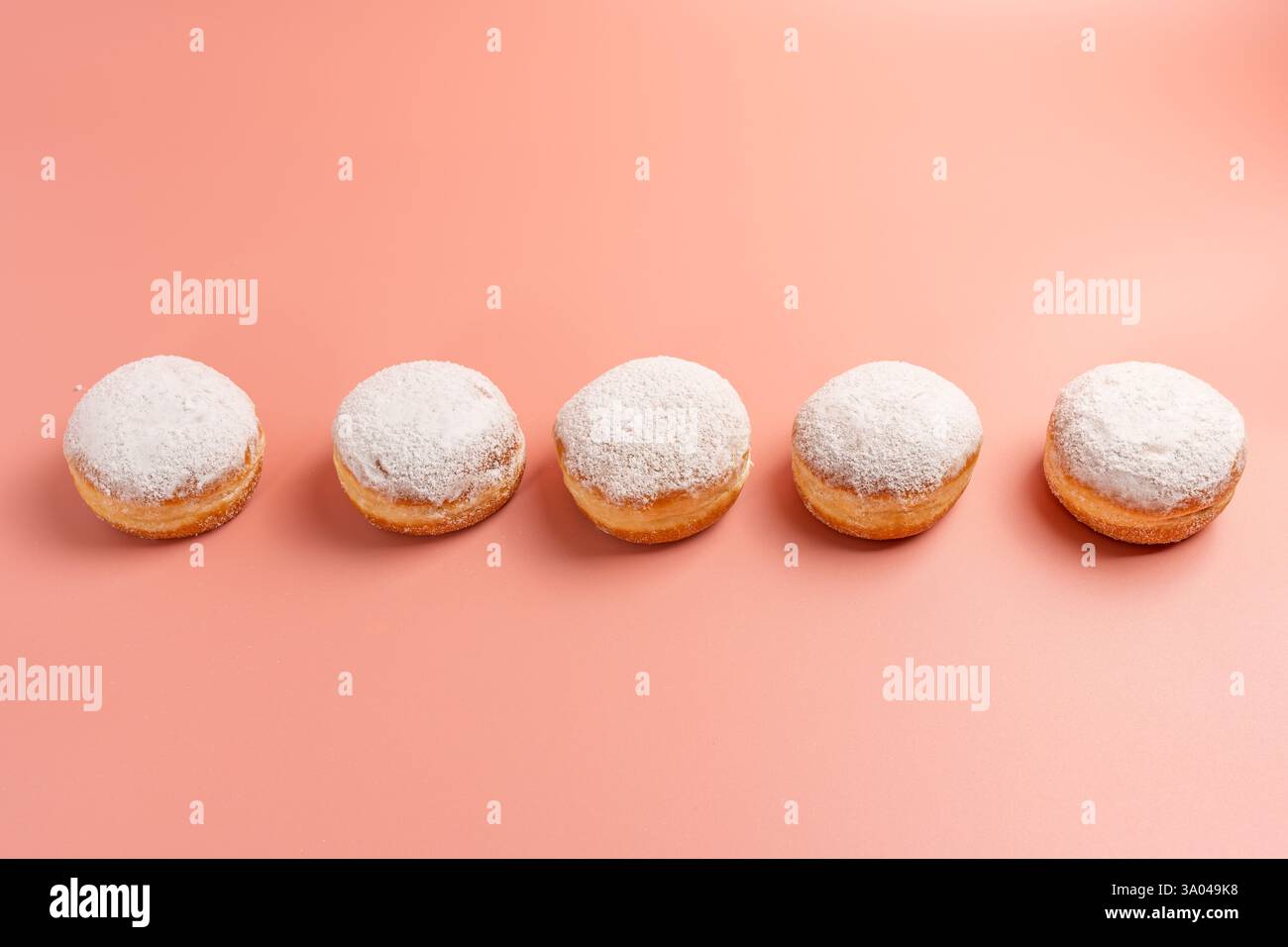 A row of five powdered donuts. The donuts are all the same size and are ...