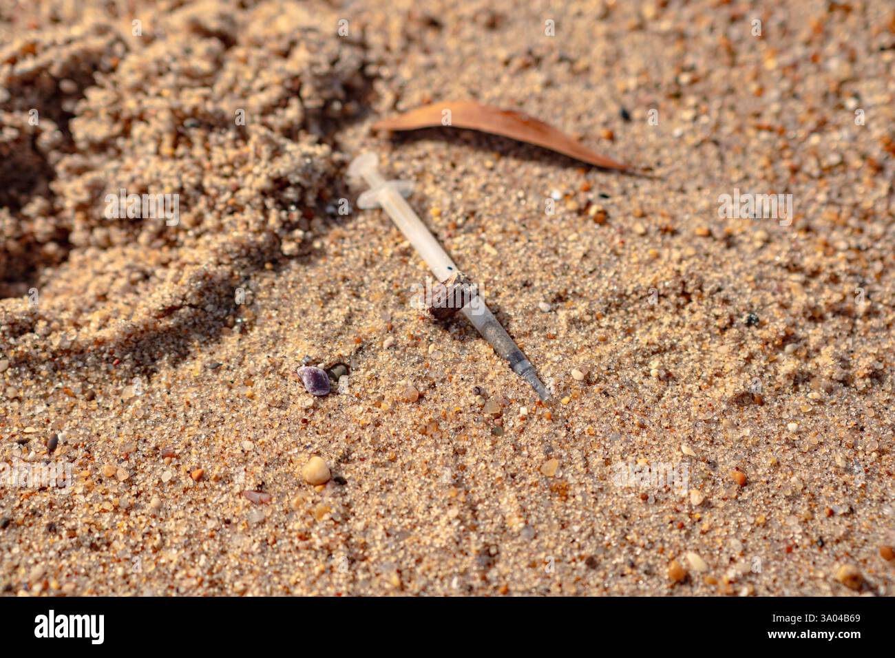 A plastic disposable syringe lies in the sand on the beach ...
