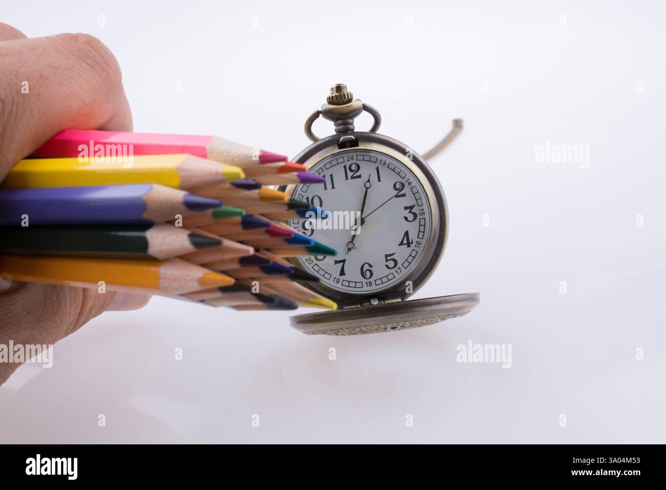 Hand holding Color Pencils beside a pocket watch on a white background ...