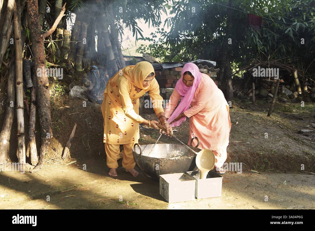 Rural women pouring boiling ingredients metal casts making washing soap ...