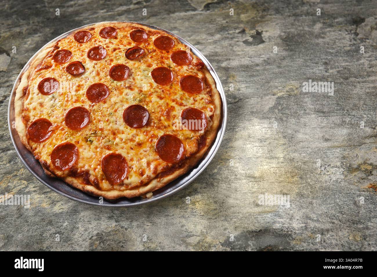 A freshly baked homemade pepperoni pizza on a slate table top, with ...
