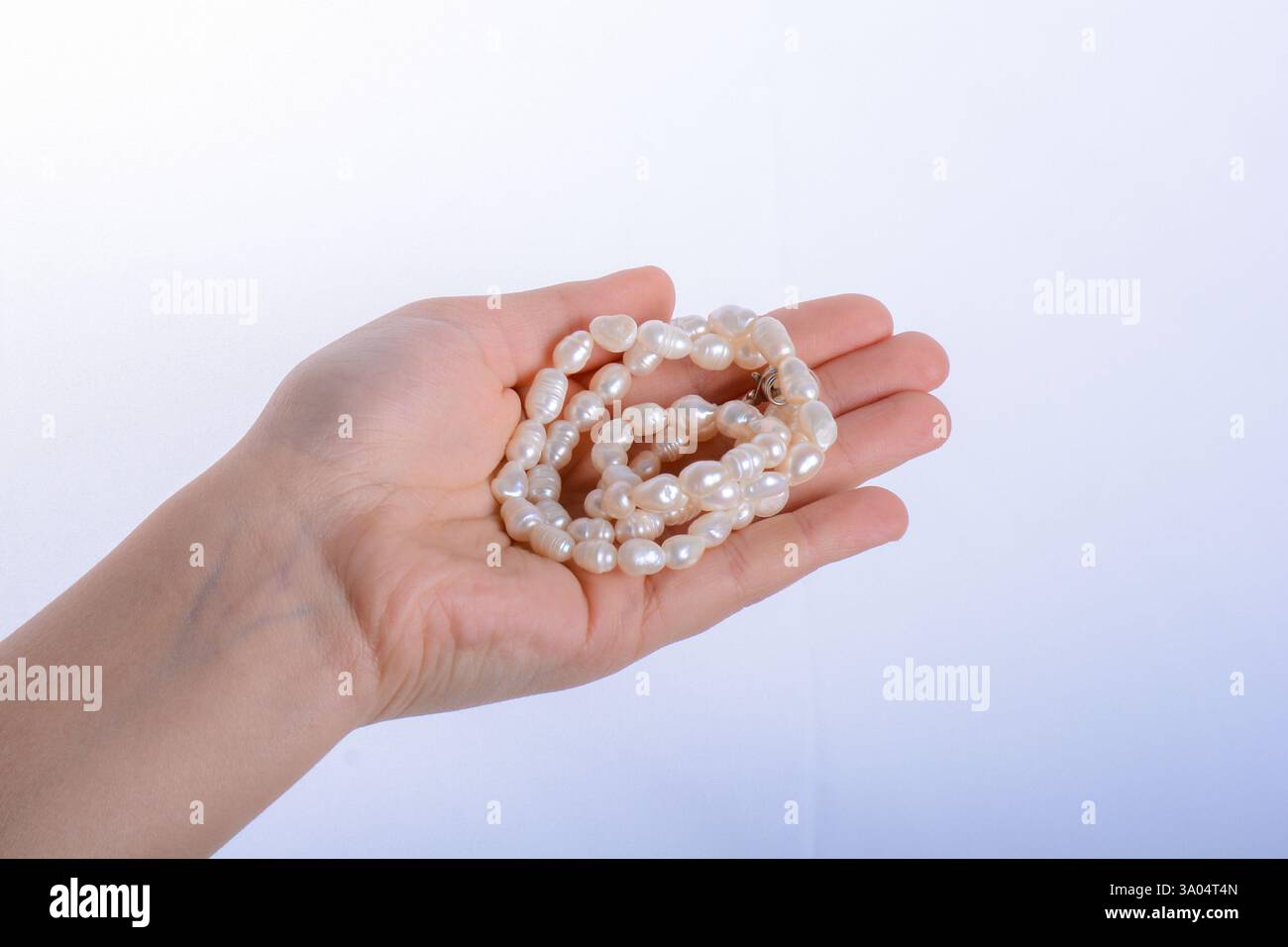 Hand holding a pearl necklace on a white background Stock Photo - Alamy