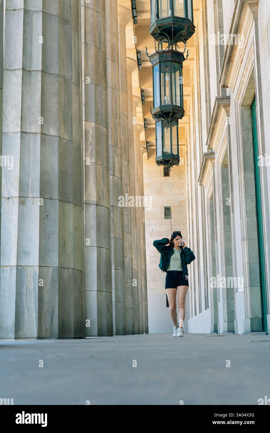 Stylish latin woman walks through a corridor adorned with columns and ...