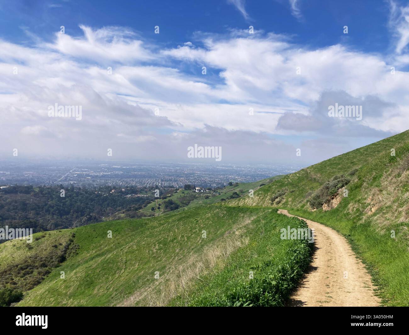 A winding dirt trail cuts through vibrant green hills, leading to ...