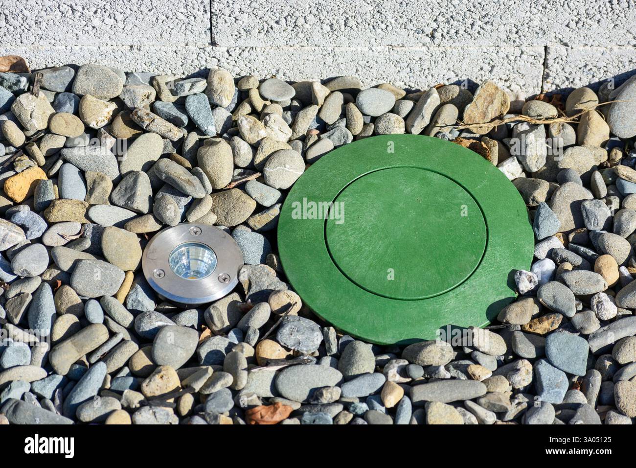 Green pop-up drainage emitter installed on a pebble-covered surface ...