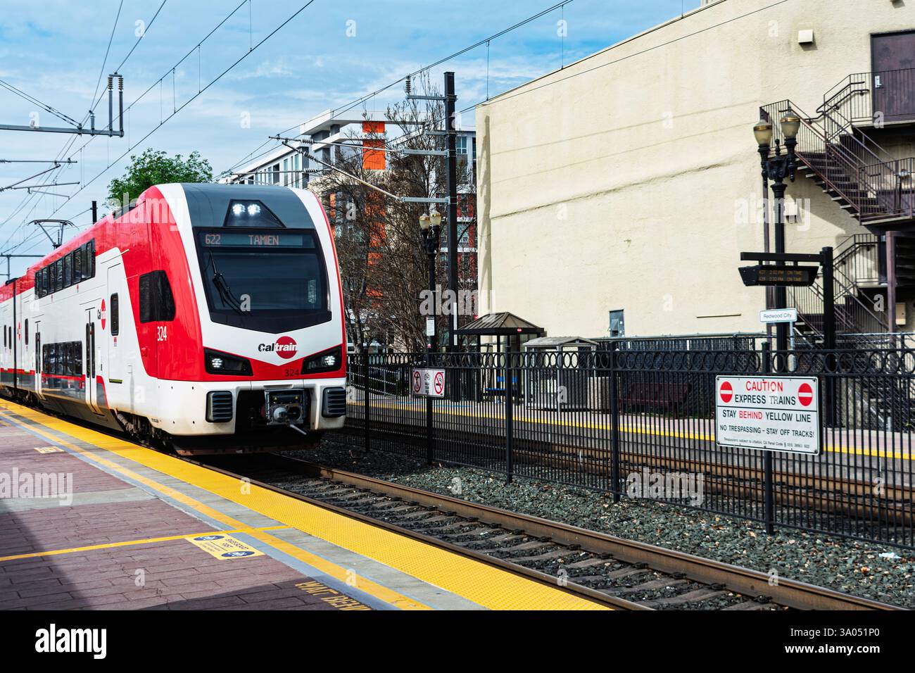Double-decker Caltrain electric train approaches a station. A fenced ...