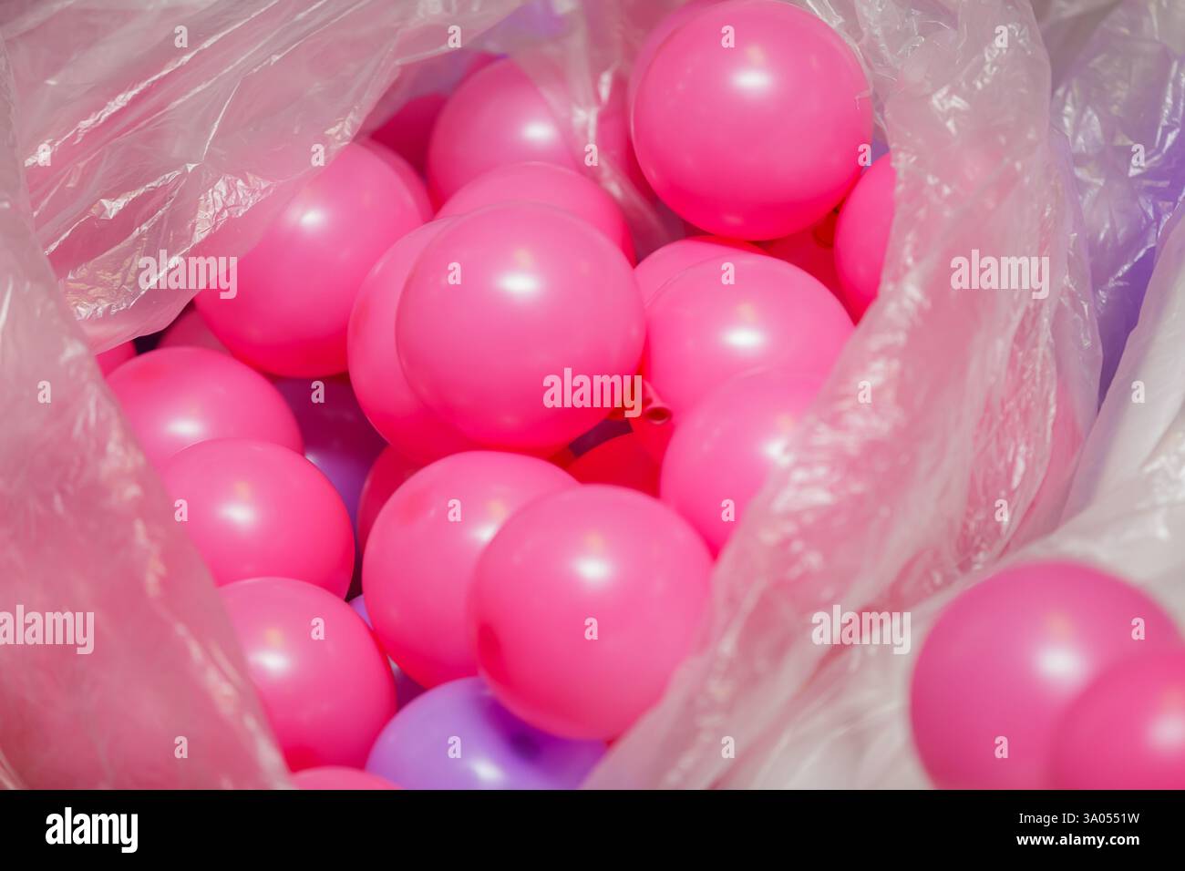 Vibrant pink plastic balls are overflowing from a clear plastic bag ...