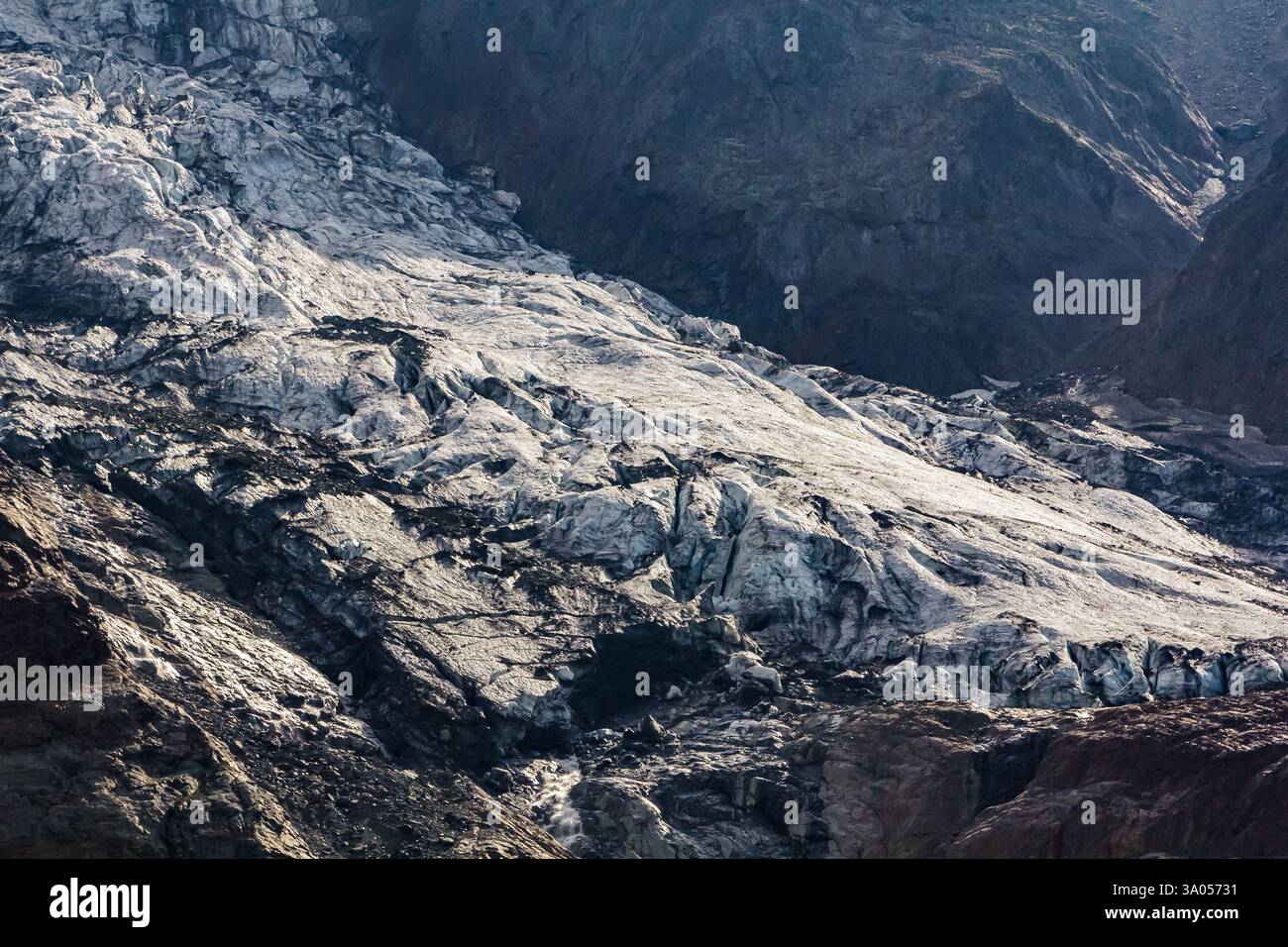 Melting glacier ice reveals dark rocks and crevasses, illustrating ...