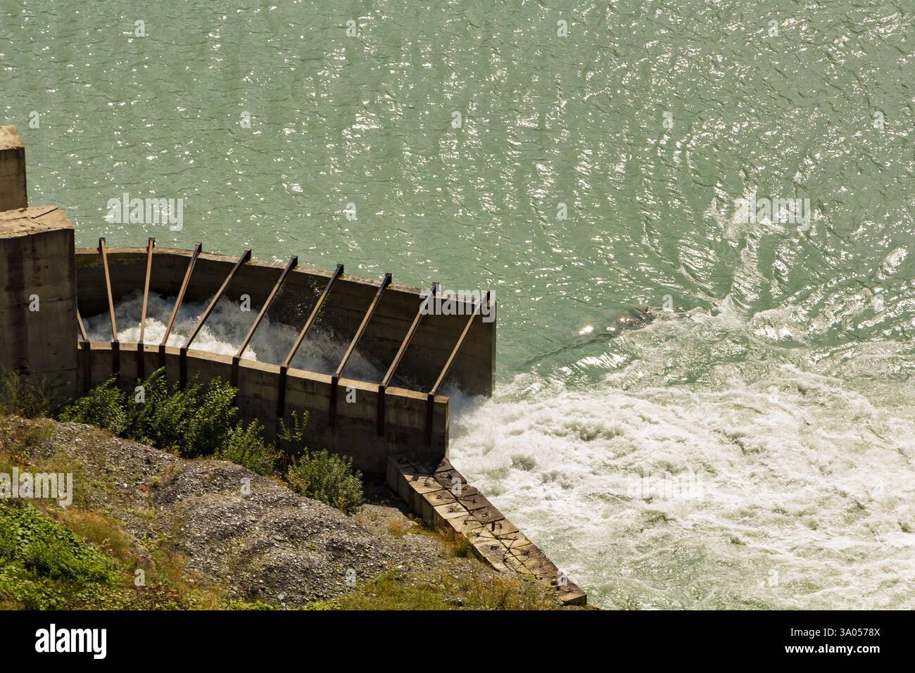 Water flows through the spillway of a dam into a river, creating ...