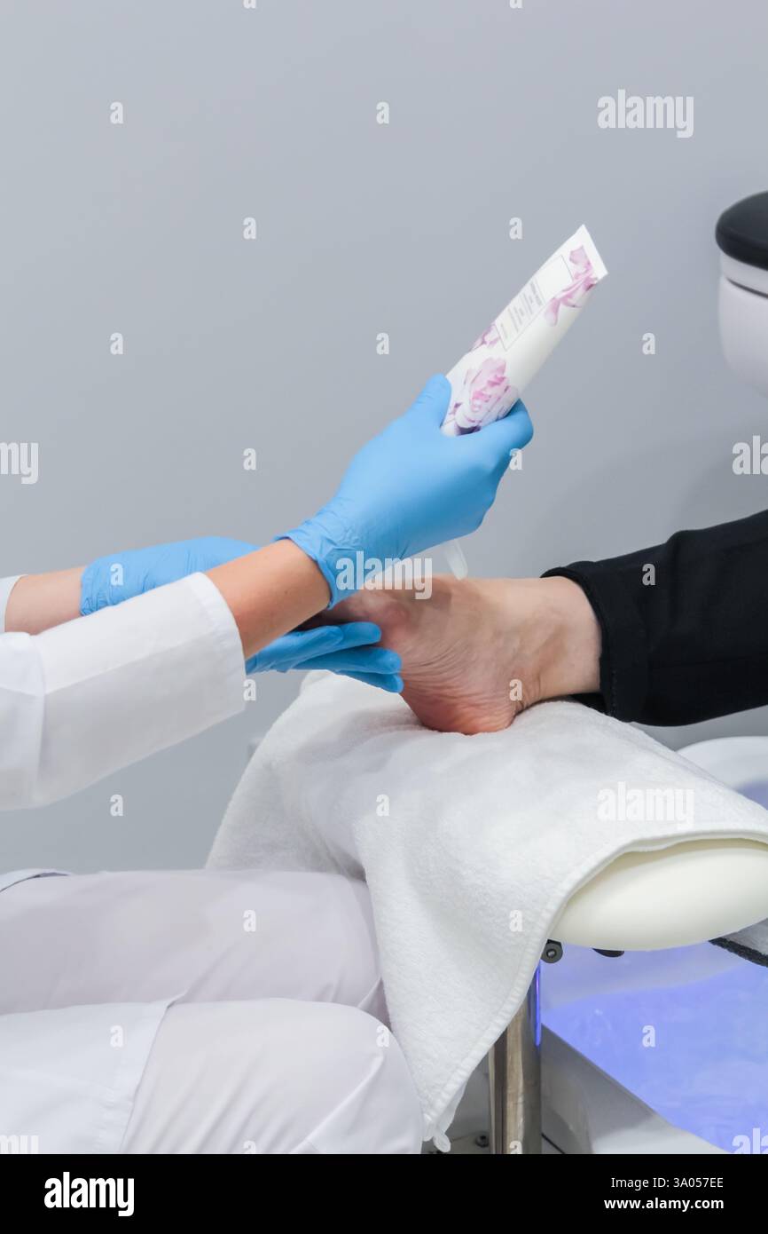 Beautician wearing gloves applying moisturizing cream on client's foot during a pedicure ...
