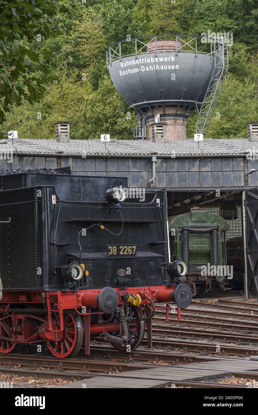 Old locomotive in front of a roundhouse with a large water tower in a ...