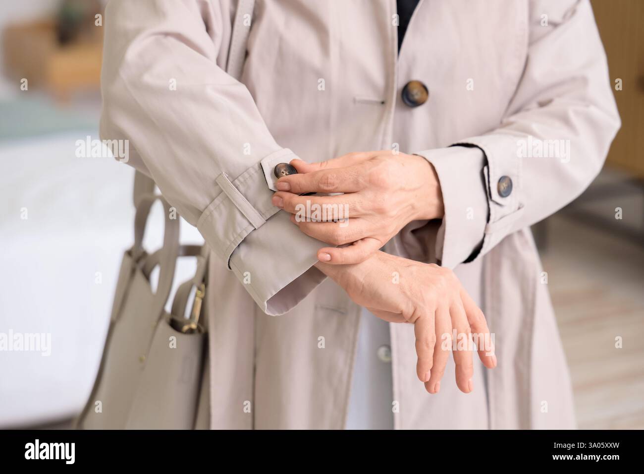 Mature woman buttoning up sleeve of trench coat at home, closeup Stock ...