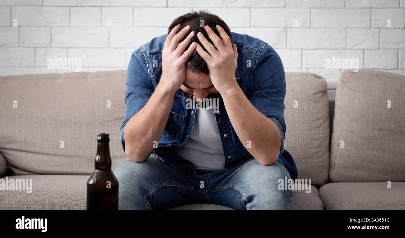 A man sits on a couch with his head in his hands, showing distress Stock Photo - Alamy