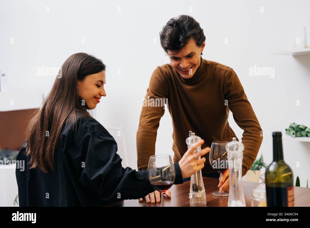 A couple smiles and shares a light moment while pouring wine at a cozy ...