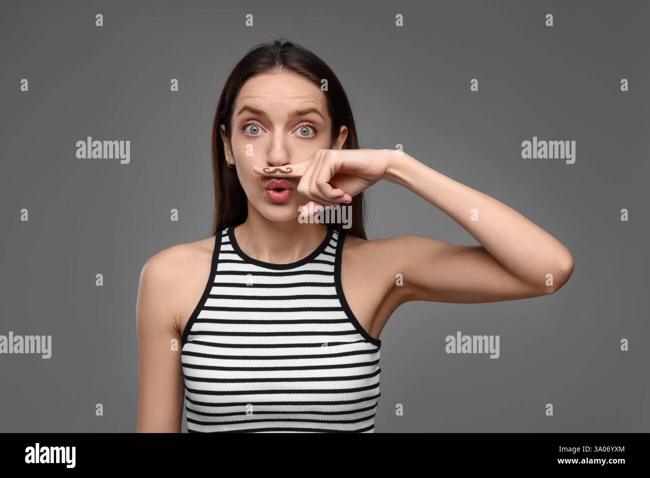 Funny woman holding finger with drawn mustache above lips on grey ...