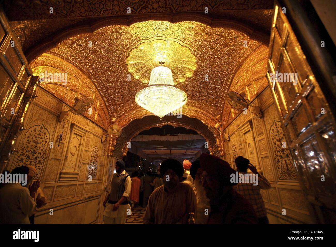 Devotees standing under chandelier in Harmandir Sahib or Darbar Sahib or Golden temple in ...