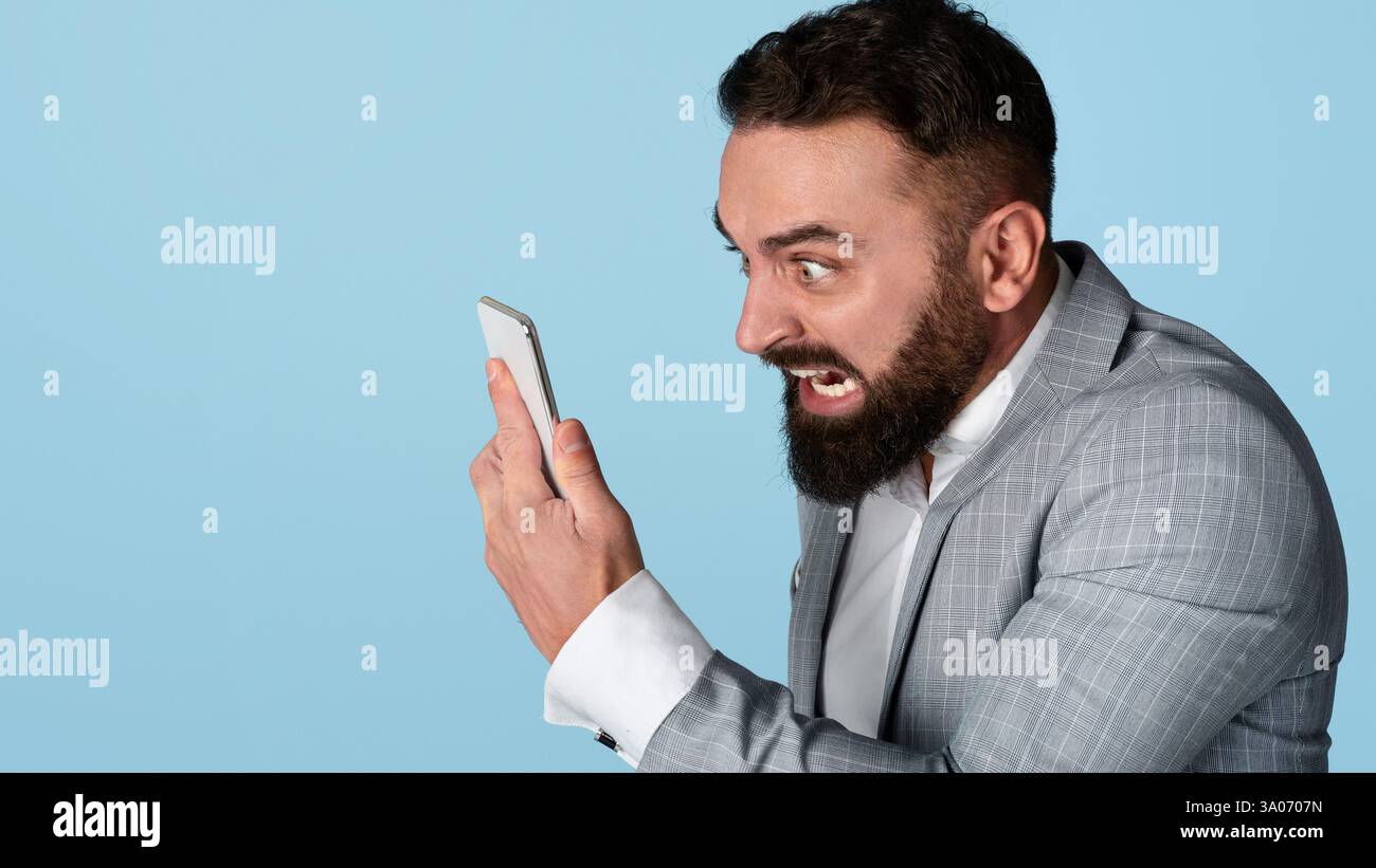 Angry young manager shouting at smartphone in fury on blue background ...