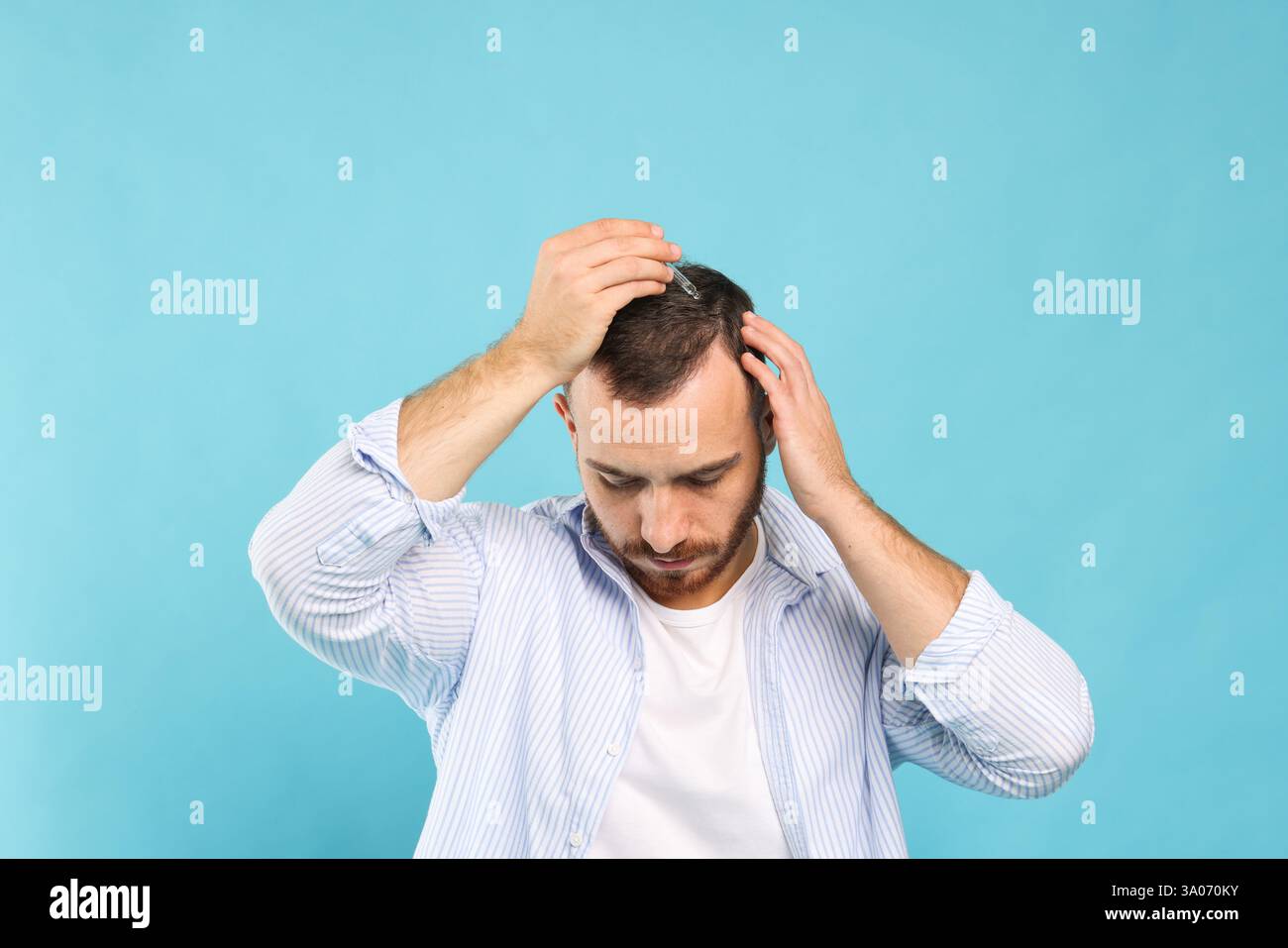 Baldness treatment. Man applying serum onto hair on light blue ...