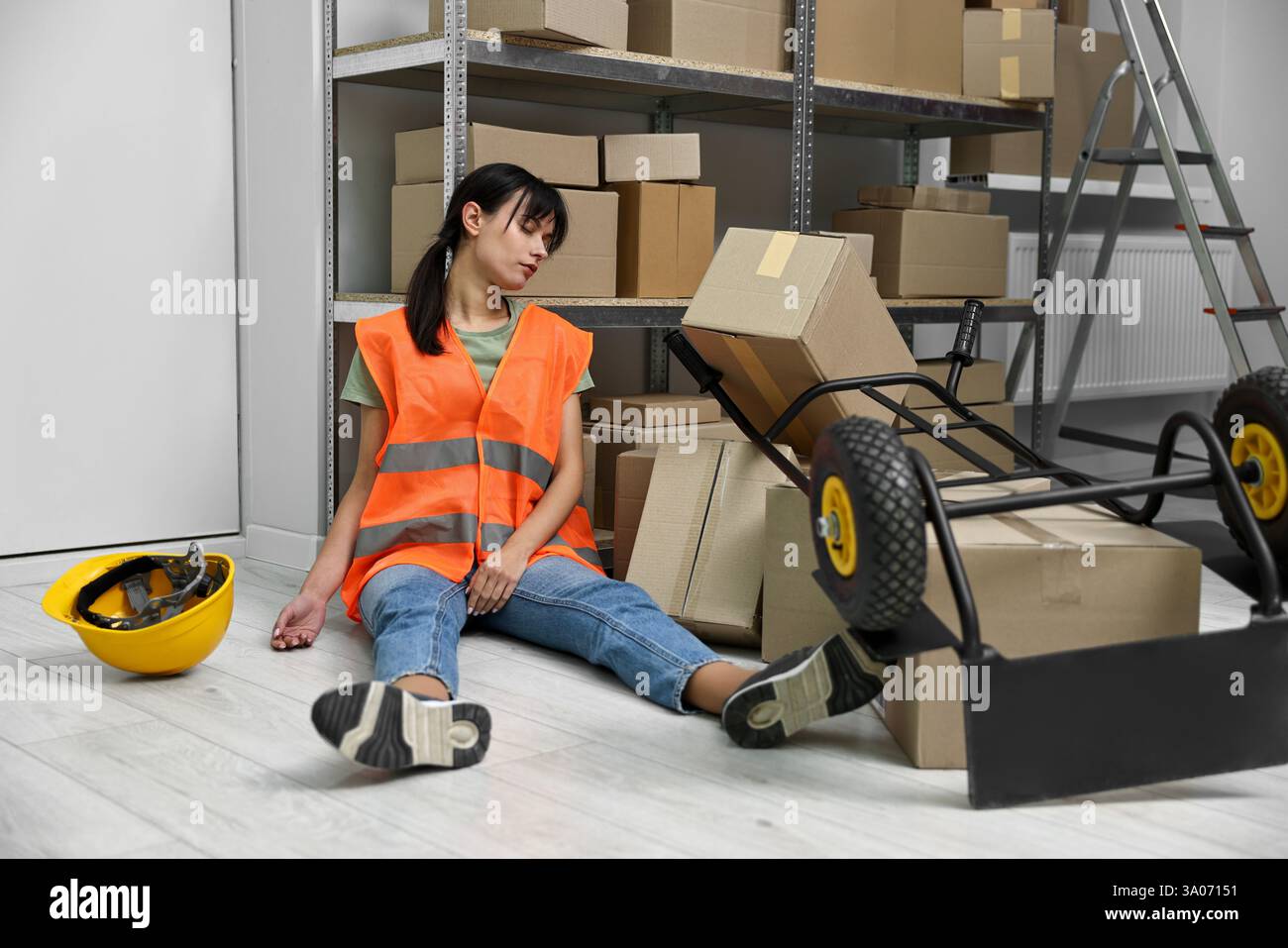 Accident at work. Unconscious woman and overturned hand truck on floor ...