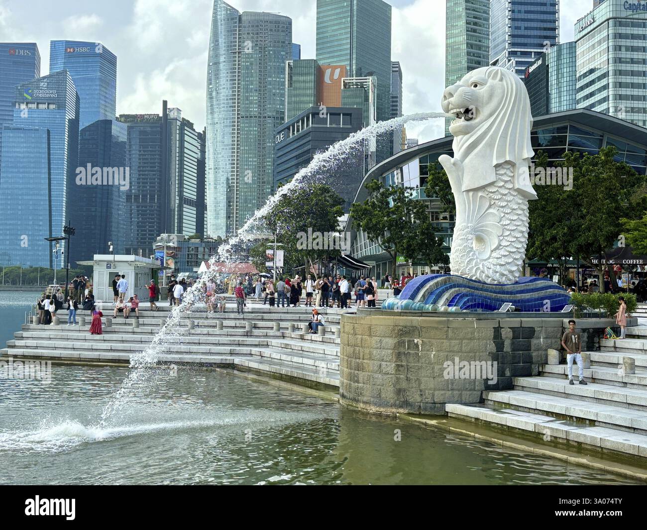 Merlion fountain with water jet in front of modern skyline and people ...
