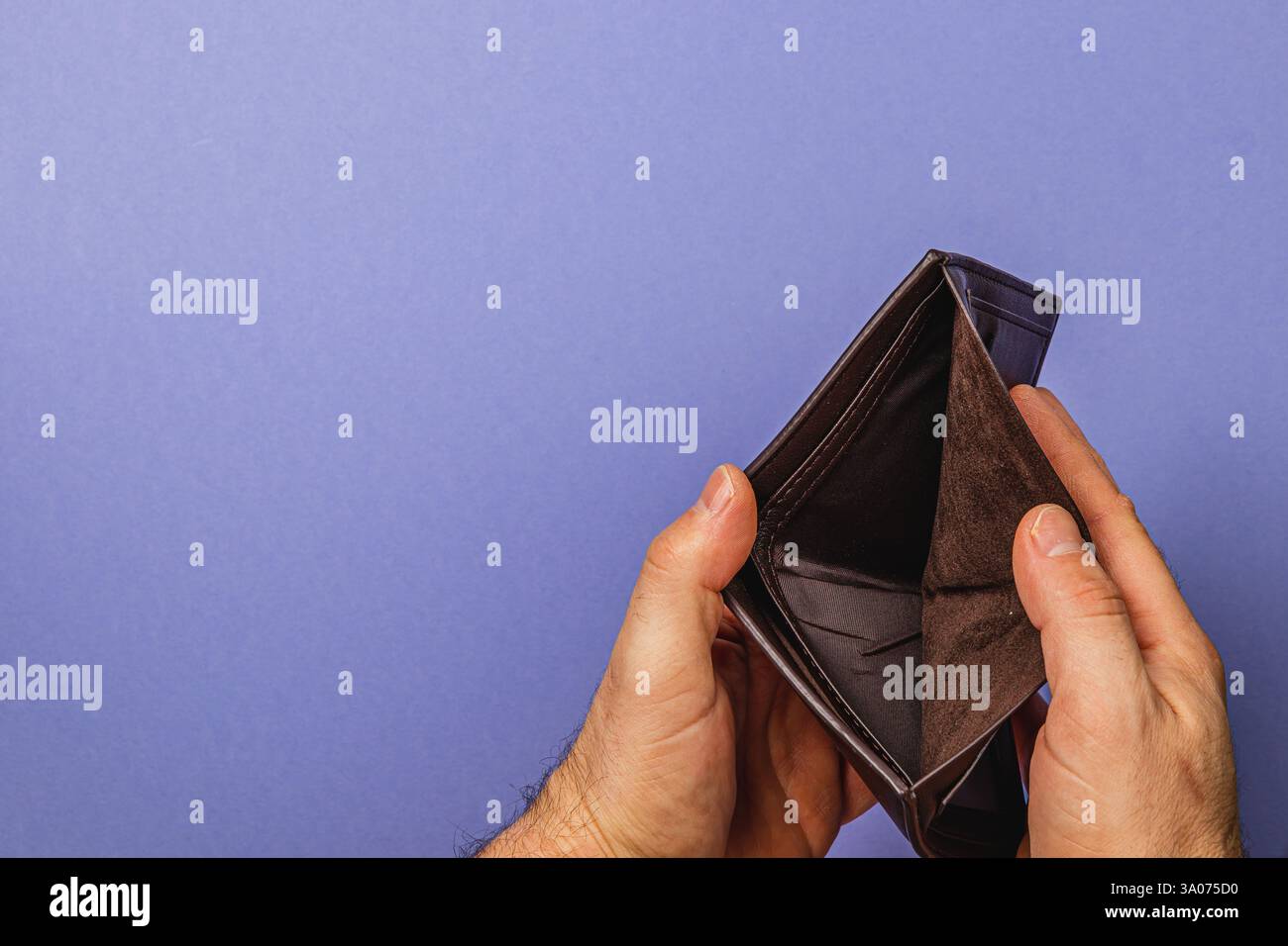 A man examines his empty wallet with a worried expression, symbolizing ...