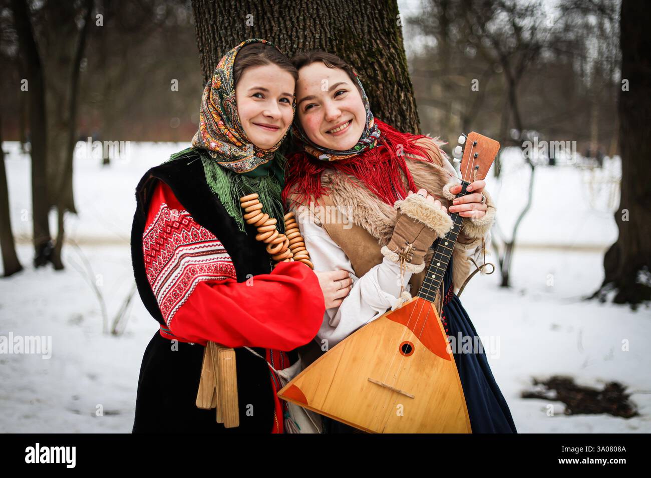 Girls in traditional Russian folk costumes stand by a tree with a ...