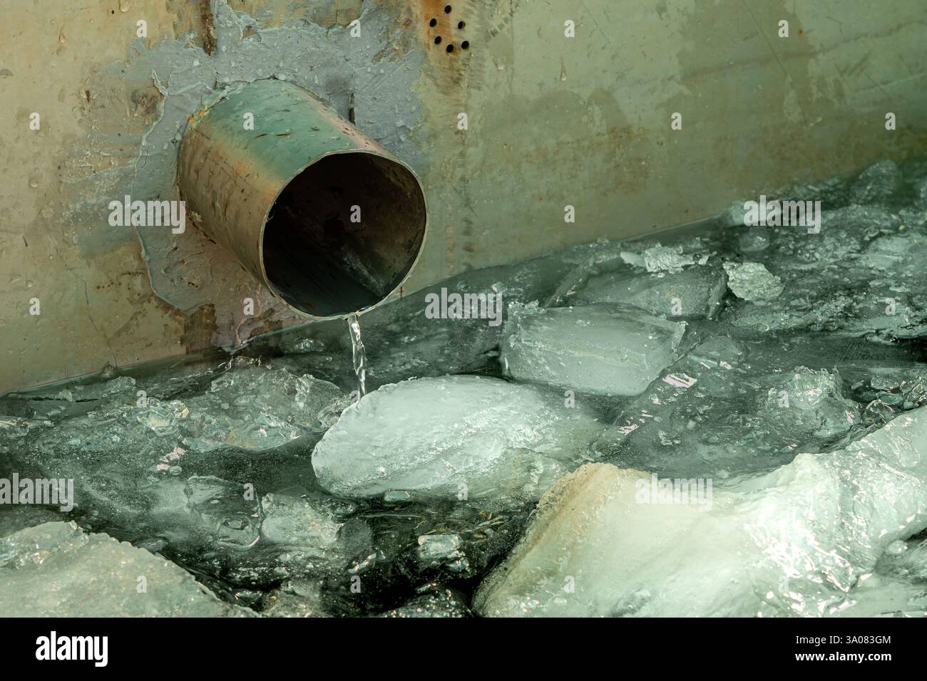 Water flows in a thin stream from a steel pipe into a reservoir filled ...
