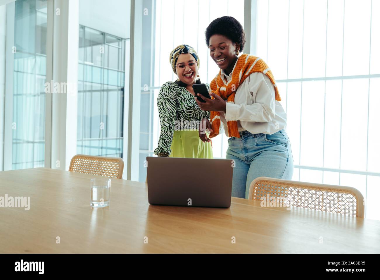 Two successful female business partners engaged in a collaborative moment, laughing and sharing ...
