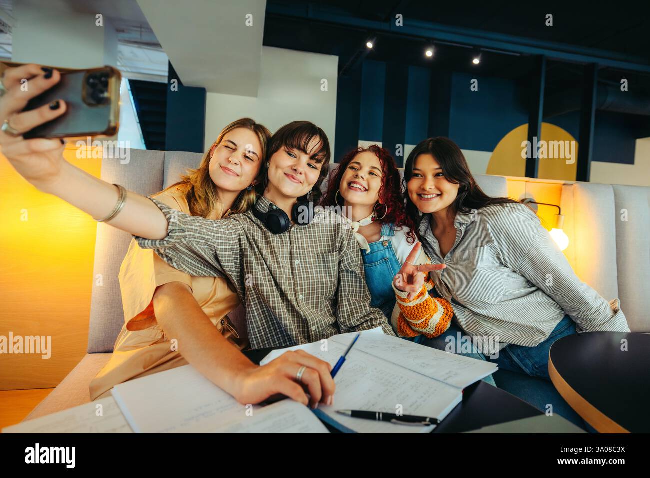 Four female college classmates capture a cheerful selfie while studying ...