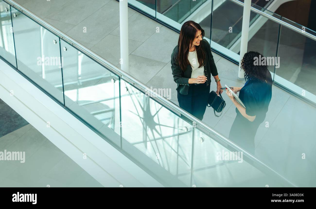 Two businesswomen engage in a friendly conversation while walking ...