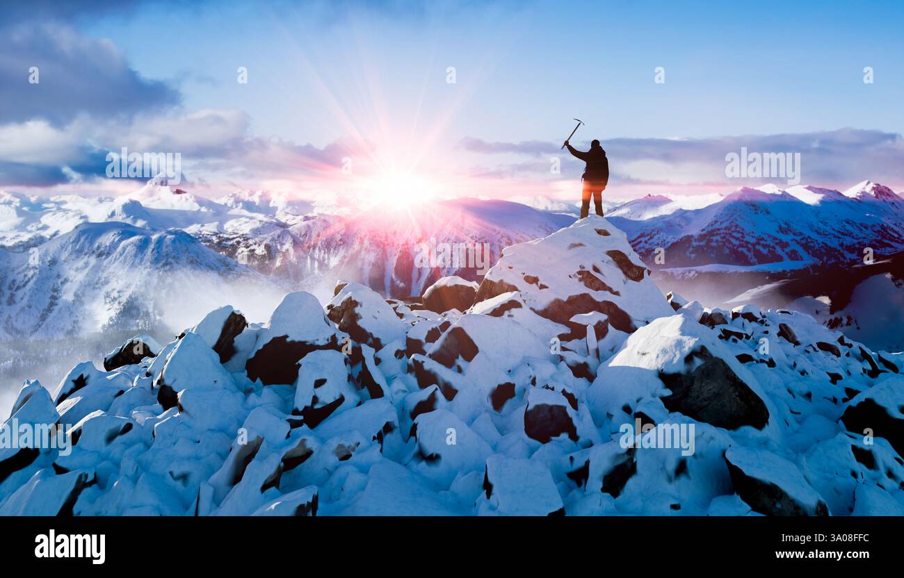 Mountaineer reaching summit of snow covered peak raising ice axe at ...