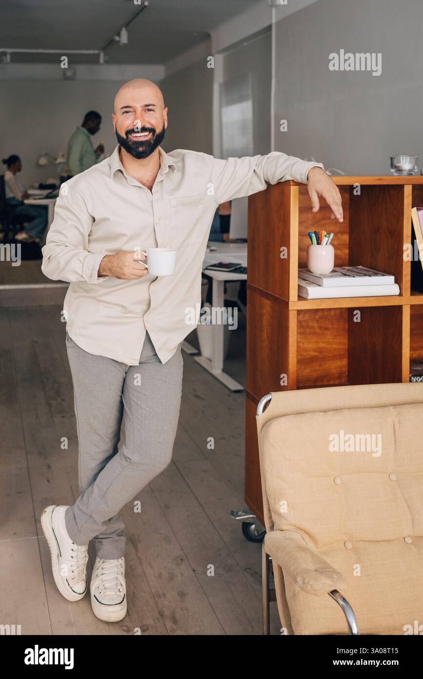 Portrait of smiling male entrepreneur holding coffee cup while leaning ...