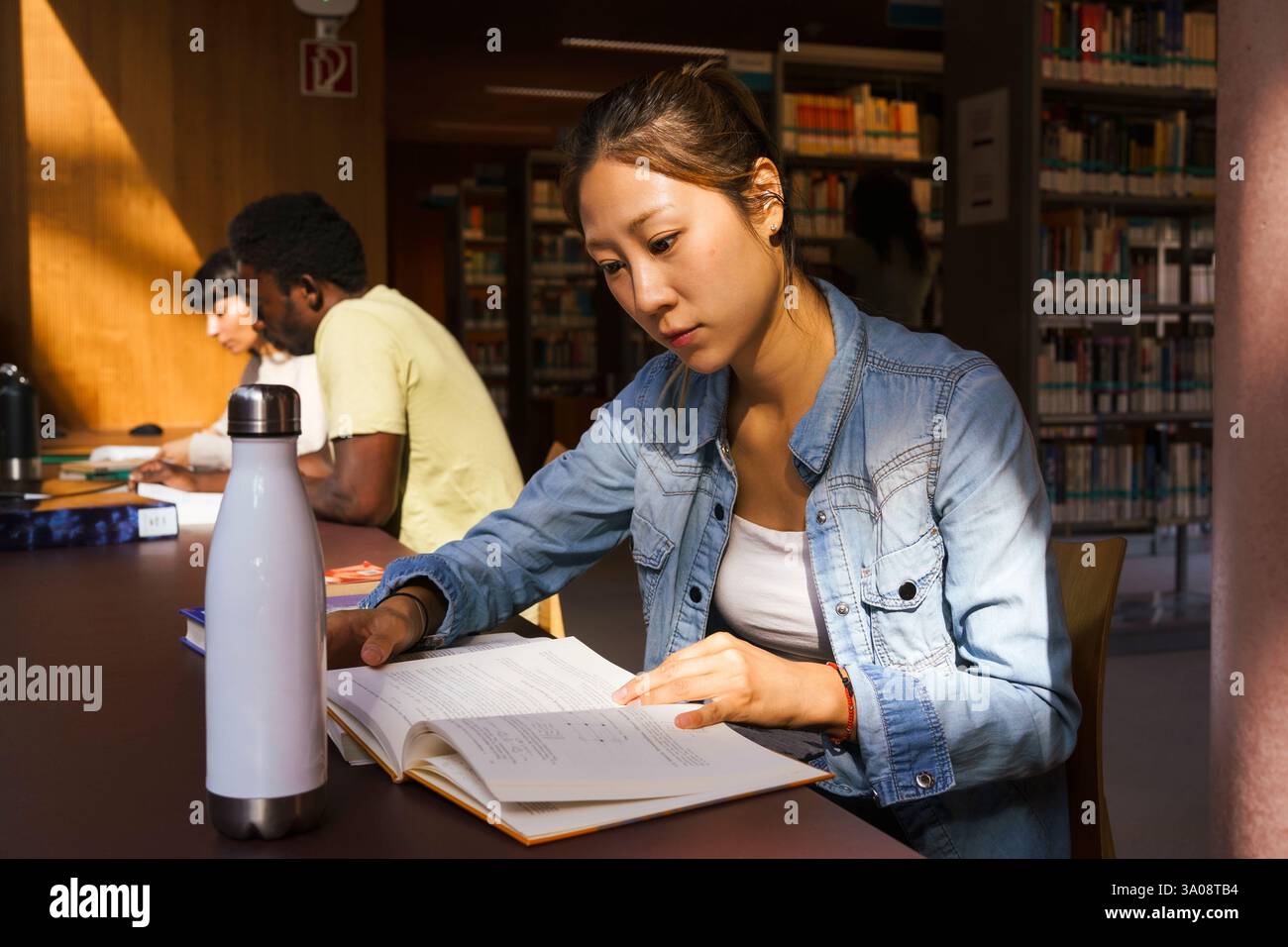 Confident female university student reading book while sitting at desk ...