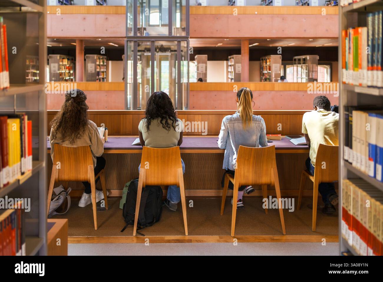Full length rear view of multiracial students sitting on chairs in ...