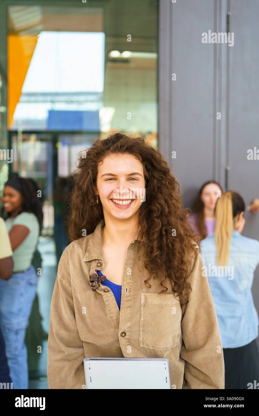 Portrait of happy young female student with curly hair standing in ...