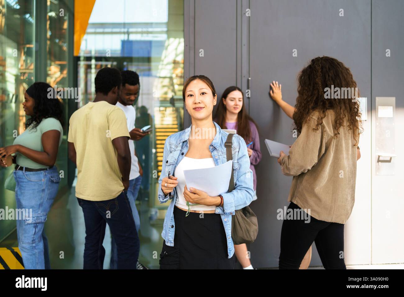 Portrait of smiling female student standing with assignment papers at ...