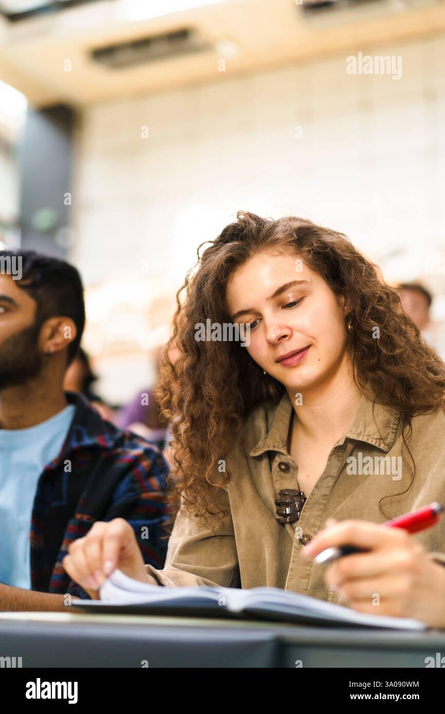 Young female student reading book and writing in lecture hall Stock ...