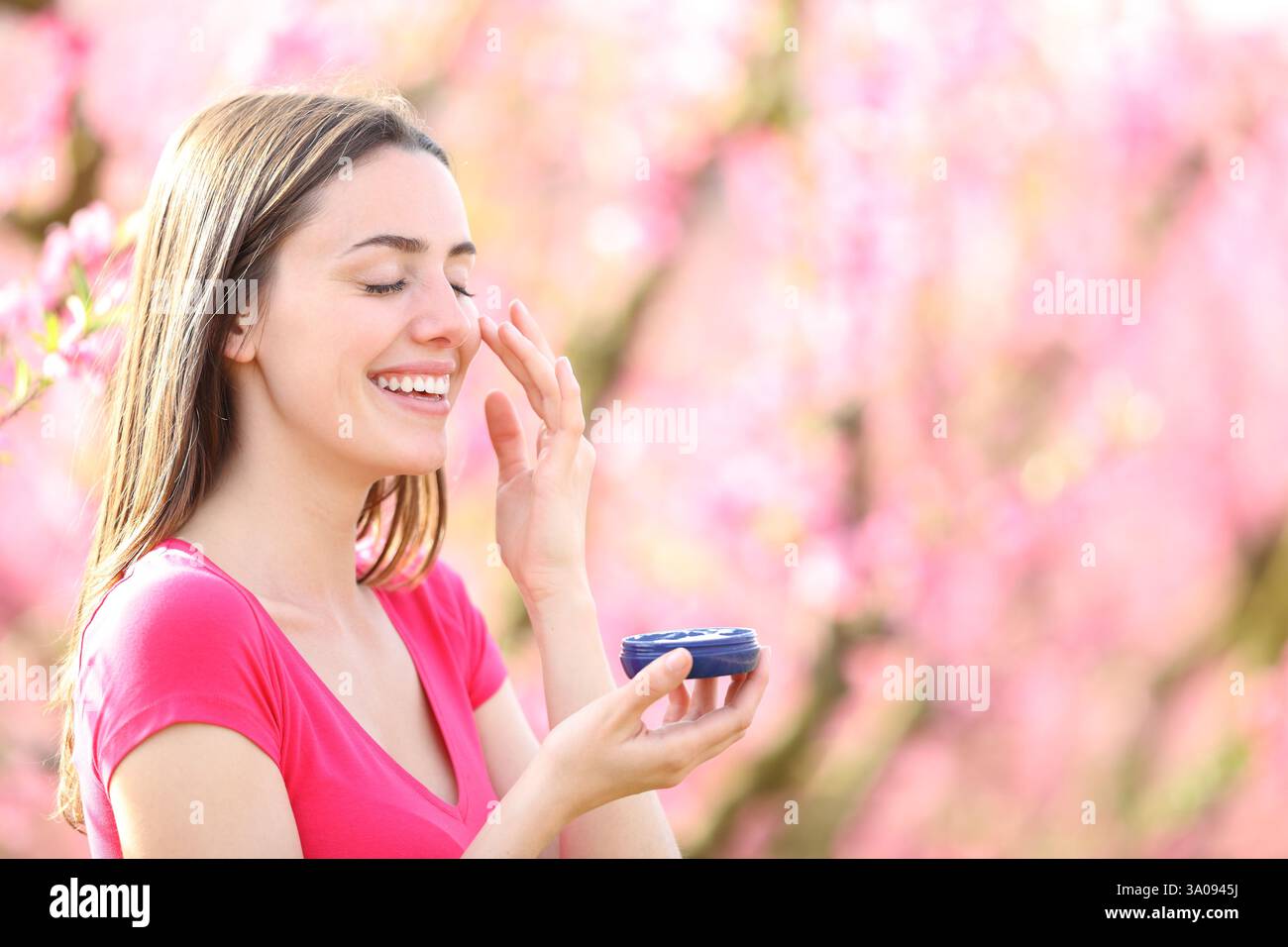 Happy candid woman applying hydration cream on cheek in a field in ...