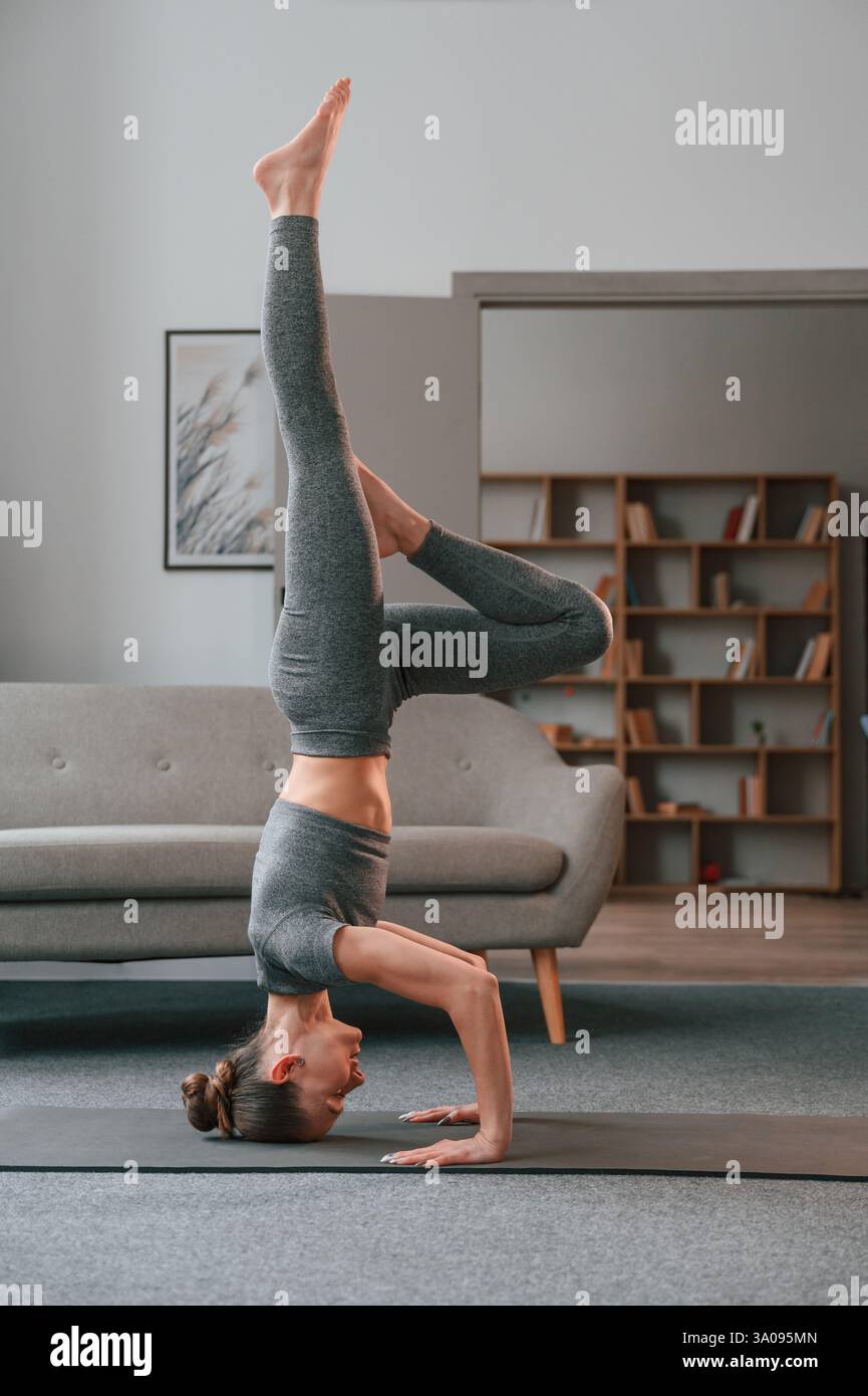Making headstand. Young woman in yoga clothes doing fitness indoors ...
