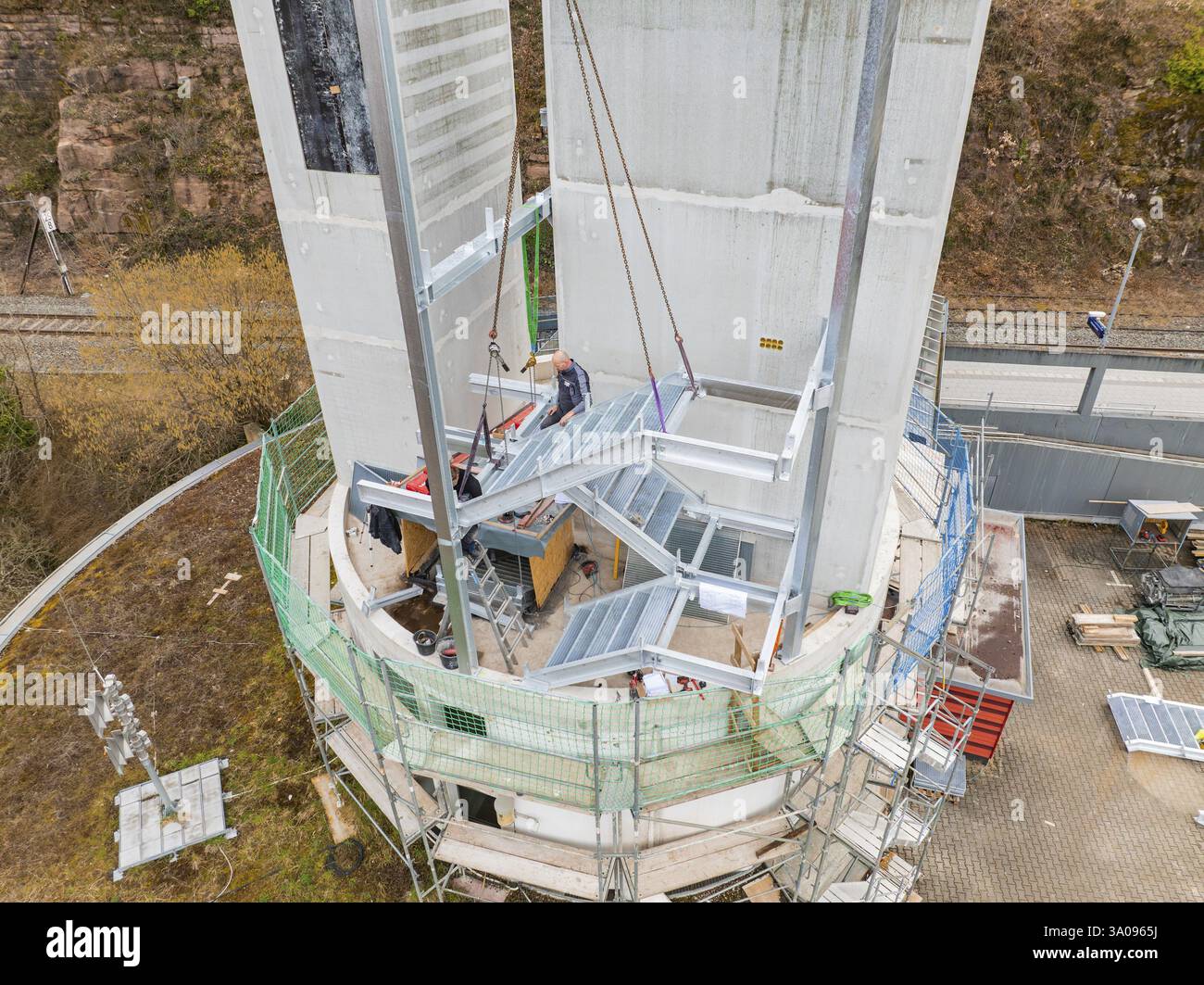 Workers use a crane to attach materials to a tall building, stairway ...