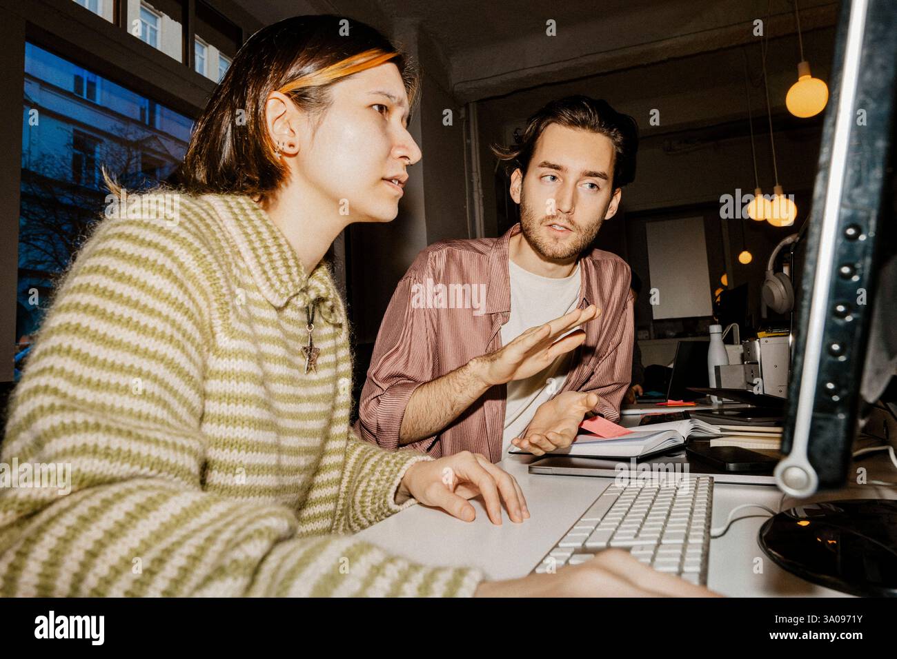 Male entrepreneur assisting female colleague working on computer at ...